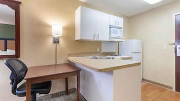 Uma kitchenette compacta com micro-ondas, geladeira e um pequeno espaço de refeições com uma cadeira e mesa.