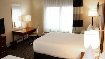 Quarto de hotel com uma cama grande, uma escrivaninha com cadeira, televisão e janela com cortinas.