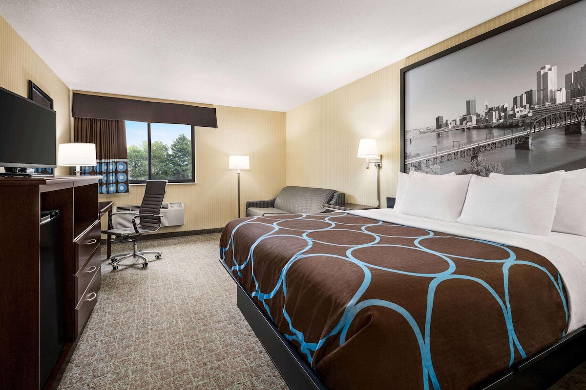 Quarto de hotel com cama, escrivaninha, cadeira, televisão e janela com vista para a cidade.