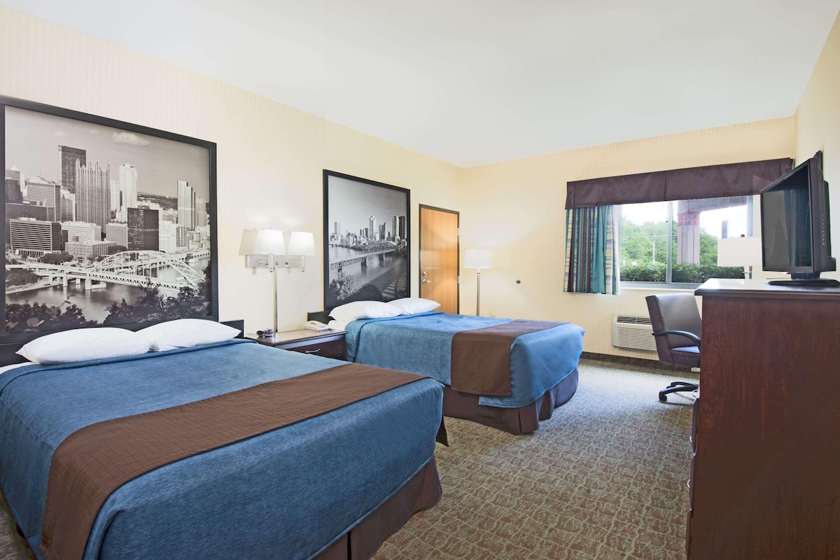 Quarto de hotel com duas camas, uma escrivaninha, uma cadeira e uma televisão.