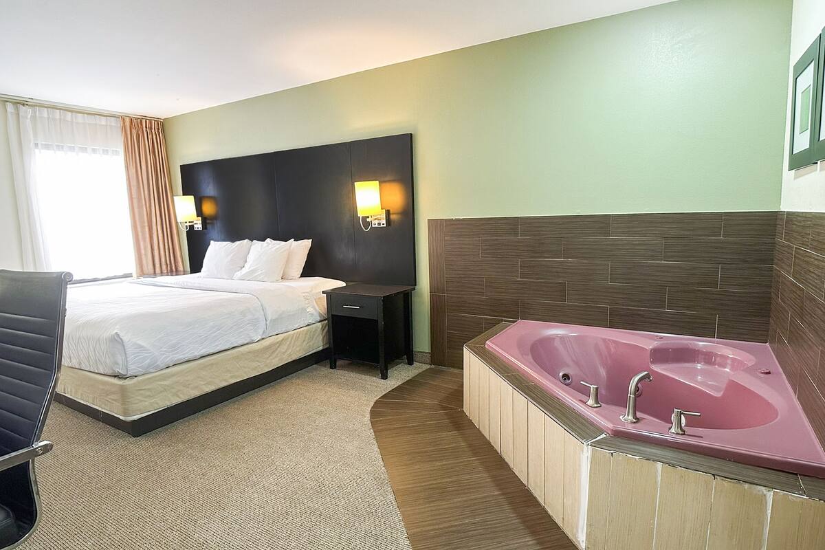 Quarto de hotel com cama, mesa de cabeceira, luminária e banheira.