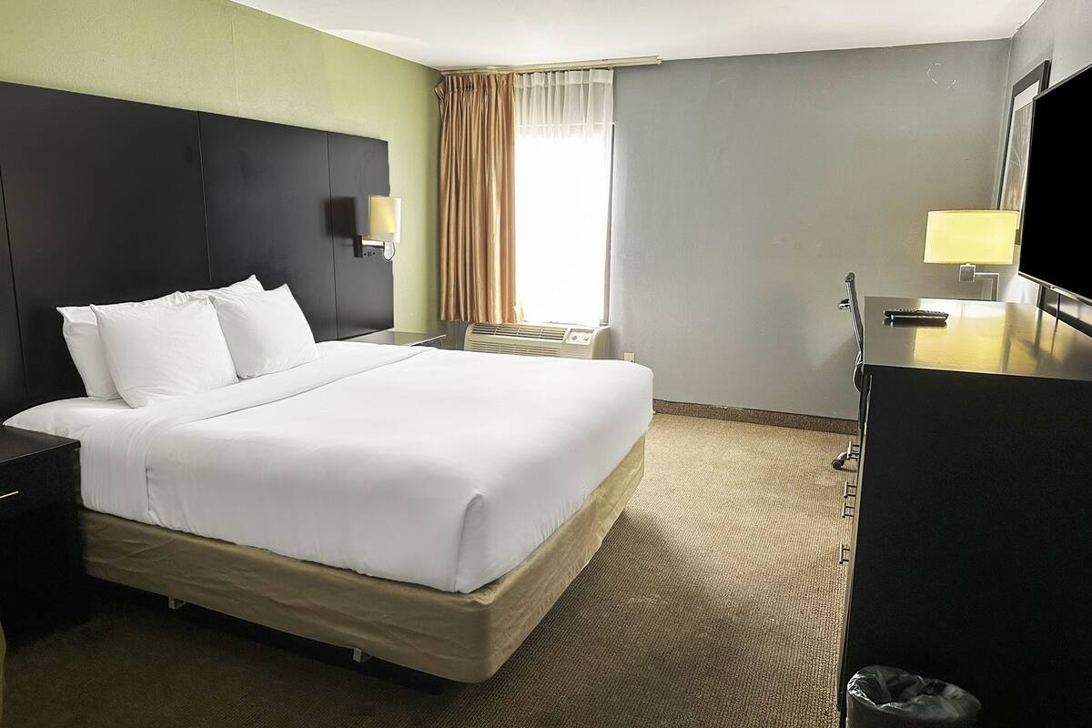 Quarto de hotel com uma cama grande, mesas de cabeceira, televisão e janela com cortinas.