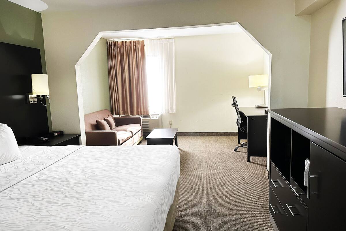 Quarto de hotel com cama grande, escrivaninha, cadeira, sofá, televisão e guarda-roupa.