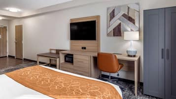 Quarto de hotel com uma cama, uma escrivaninha com cadeira, uma televisão, um guarda-roupa e um abajur.