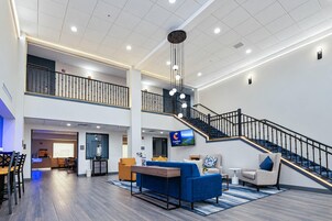 Um amplo hall de hotel com teto alto, escada e área de estar com sofá azul e mesa de centro.