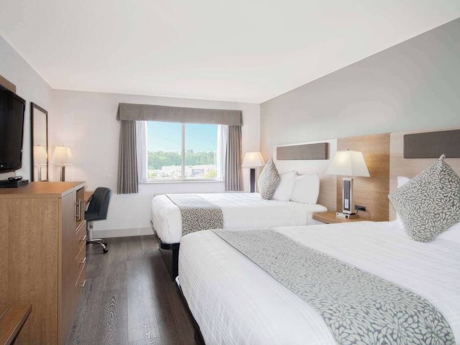 Quarto de hotel com duas camas, uma mesa, uma televisão e uma janela com vista.
