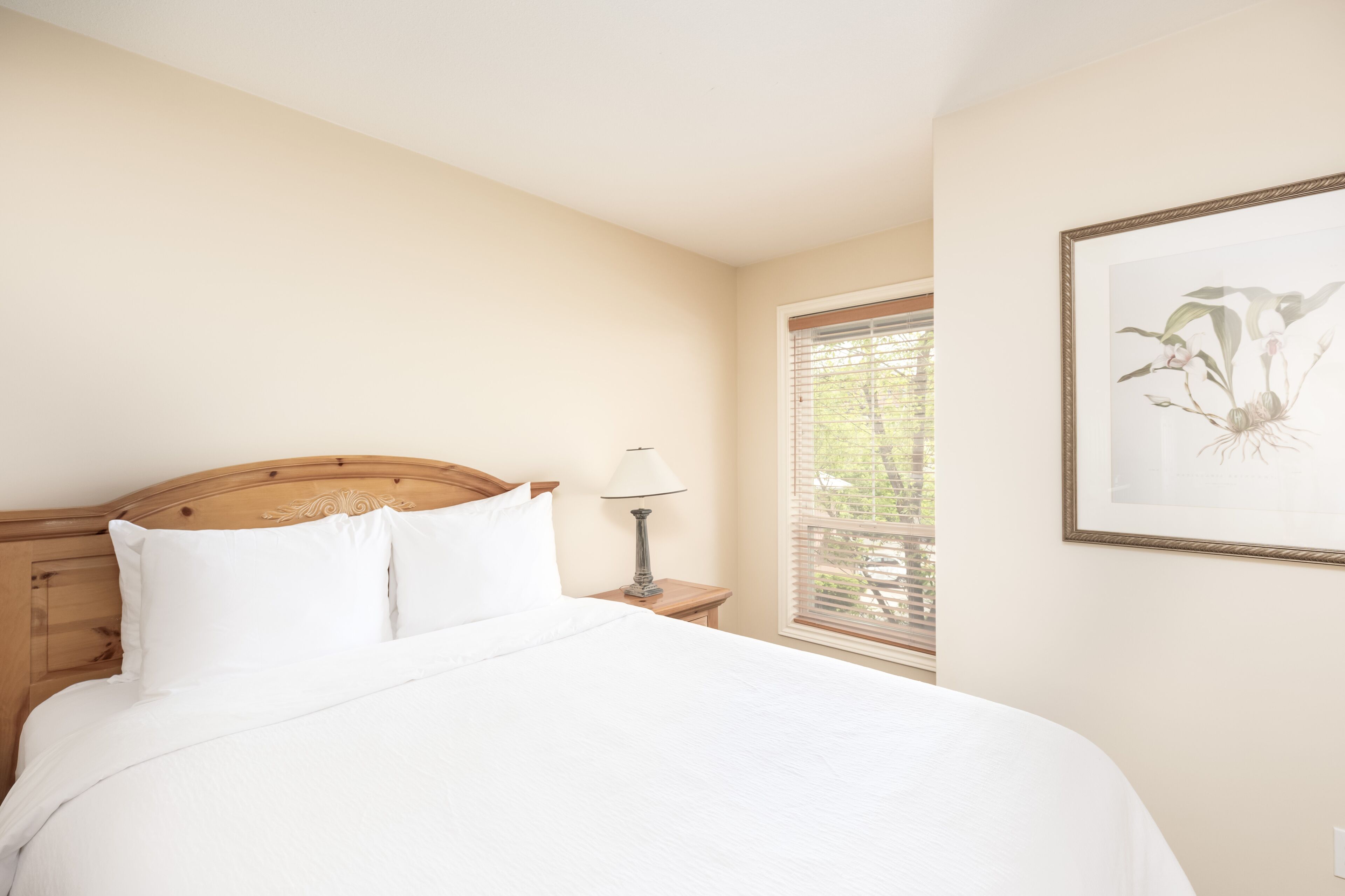 Cama bem arrumada com lençóis brancos em quarto com cabeceira de madeira, luminária de cabeceira e janela com persianas.