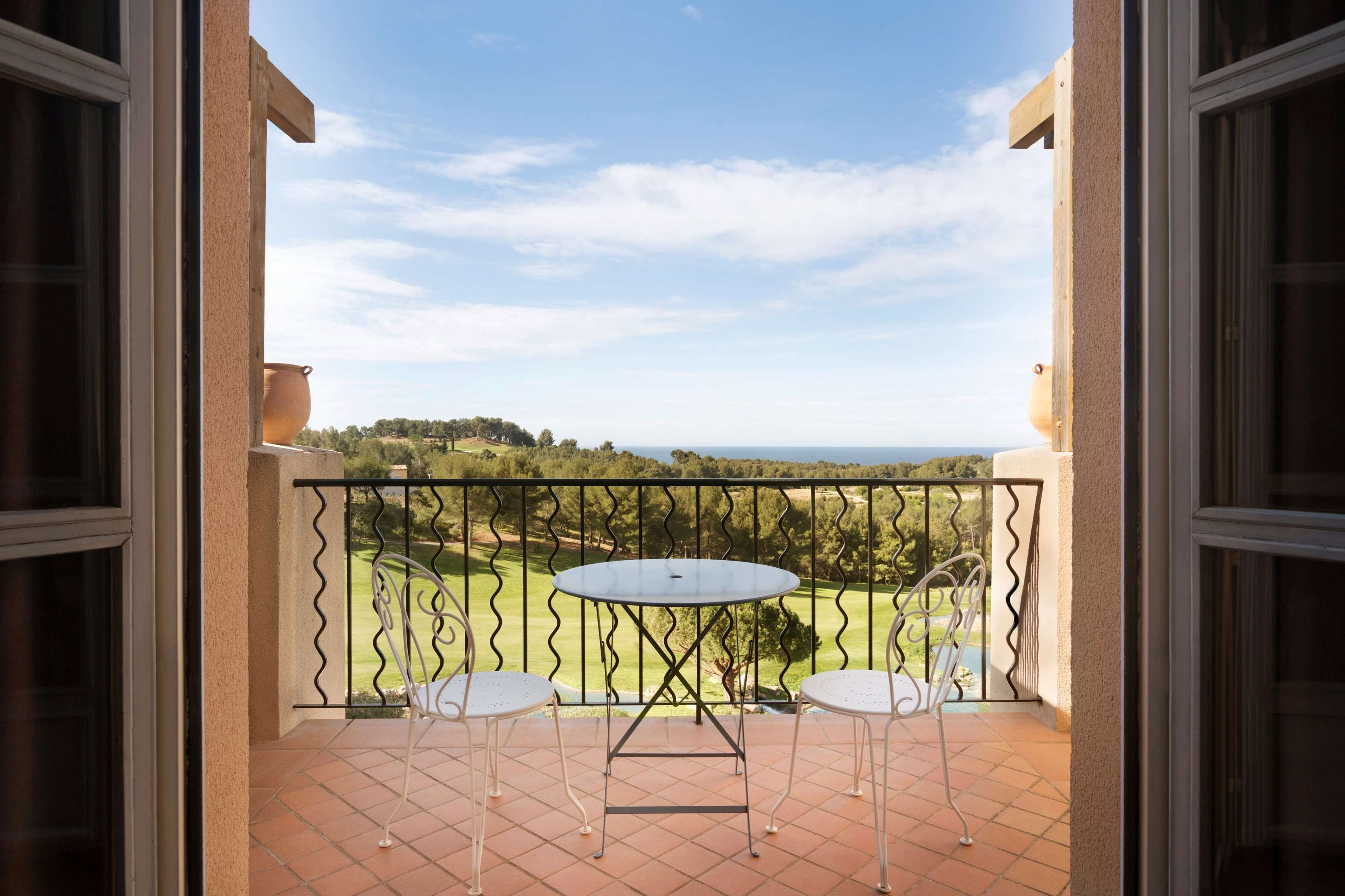 Varanda com mesa e cadeiras, com vista para um campo de golfe e paisagem distante.