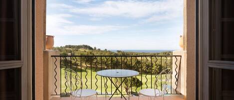 Varanda com mesa e cadeiras, com vista para um campo de golfe e paisagem distante.