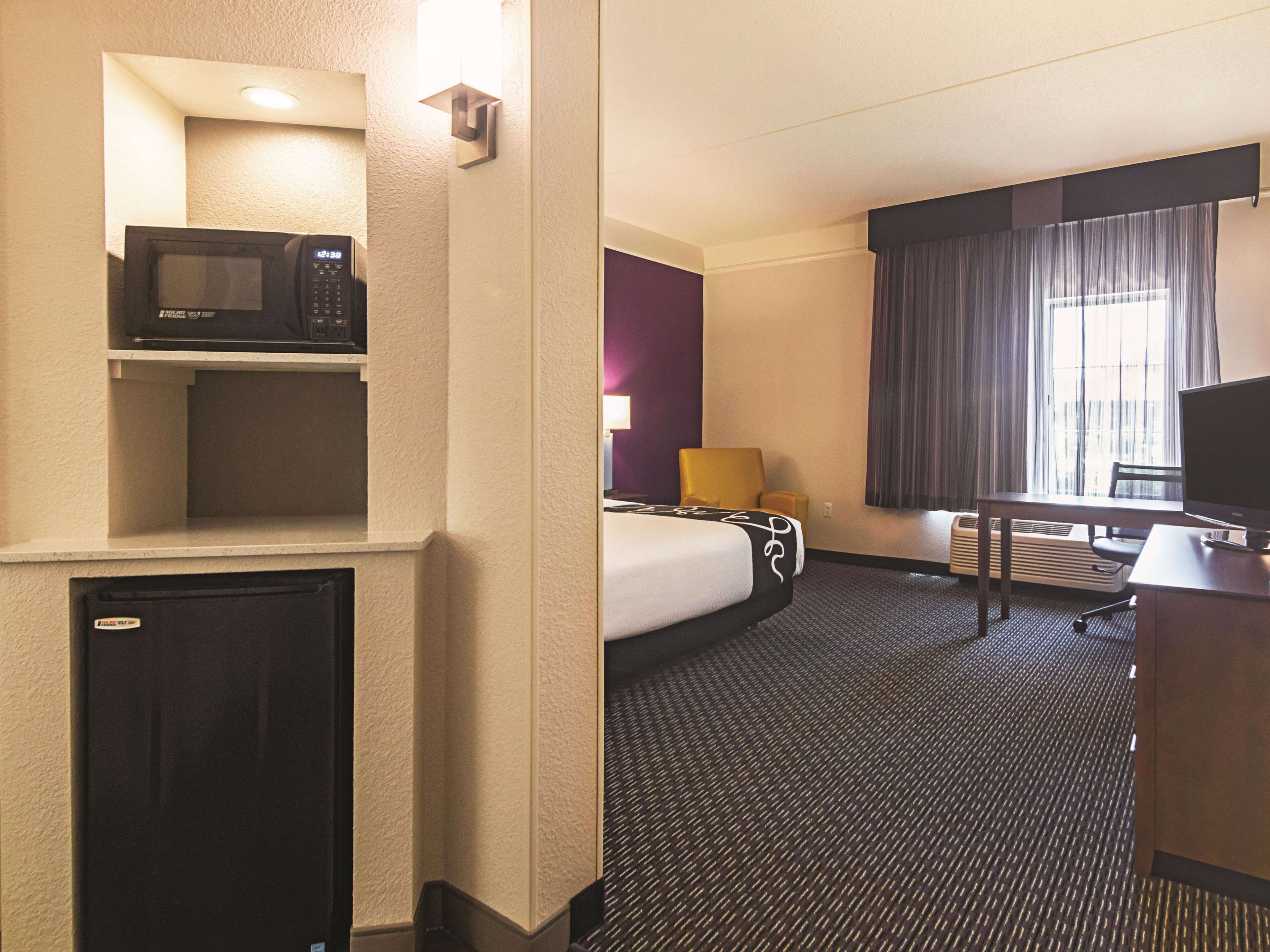 Quarto de hotel com cama, escrivaninha, computador, micro-ondas e pequeno frigorífico.