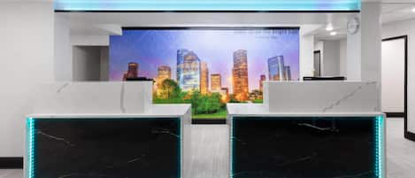 Uma área de recepção com balcões de mármore, um mural com vista para a cidade e um relógio na parede.