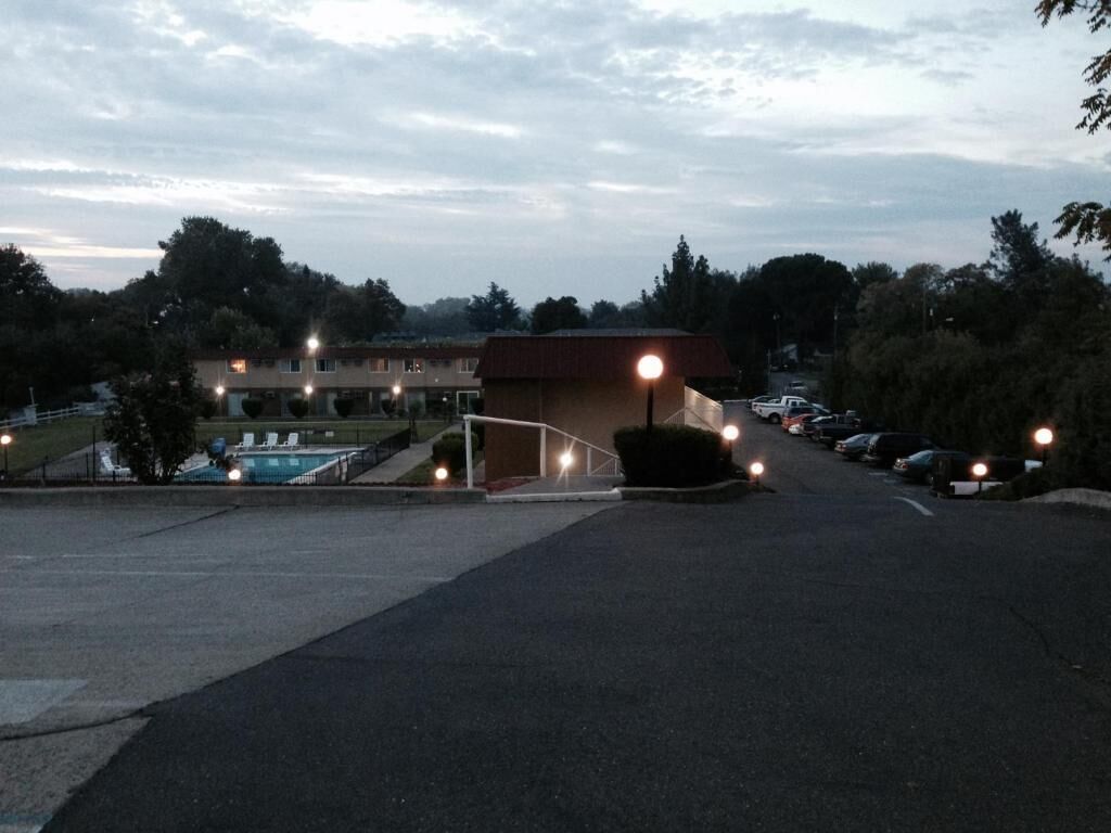 Um estacionamento com um edifício ao fundo, piscina e árvores.