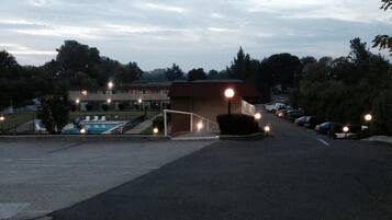 Um estacionamento com um edifício ao fundo, piscina e árvores.