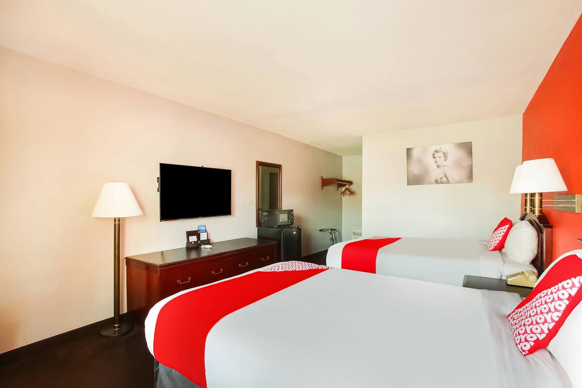 Quarto de hotel com duas camas, televisão de tela plana, escrivaninha com luminária, cômoda e micro-ondas.