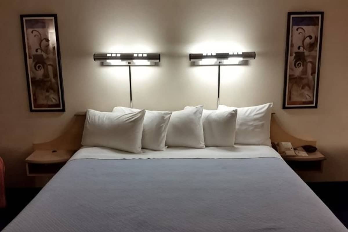 Quarto de hotel com uma cama grande, duas mesas de cabeceira, luminárias fixadas na parede e obras de arte emolduradas nas paredes.