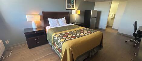 Quarto de hotel com cama, mesas de cabeceira, luminária, geladeira e escrivaninha com cadeira.