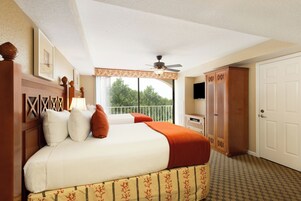 Quarto de hotel com uma cama, um ventilador de teto, janela com vista para árvores e um guarda-roupa.
