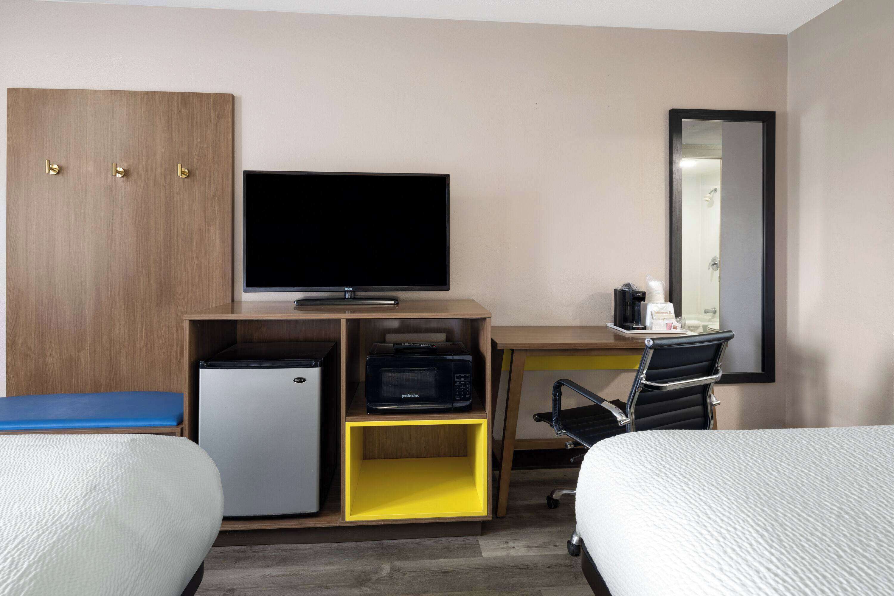 Quarto de hotel com duas camas, uma escrivaninha com televisão, micro-ondas e frigorífico.