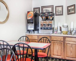 Um café com balcão, máquinas de espresso, dispensador de água e quadros pendurados na parede.
