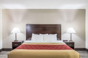 Quarto de hotel com uma cama grande, duas mesas de cabeceira com luminárias, um painel de cabeceira de madeira e um edredom vermelho estampado.