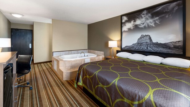 Quarto de hotel com uma cama grande, uma escrivaninha, uma cadeira, banheiro com banheira e um quadro na parede.