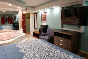 Quarto de hotel com uma cama grande, um espaço de estar com uma poltrona, televisão, micro-ondas e banheira.