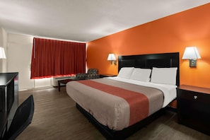 Quarto de hotel com cama, duas luminárias de cabeceira, escrivaninha com cadeira e janela com cortinas vermelhas.