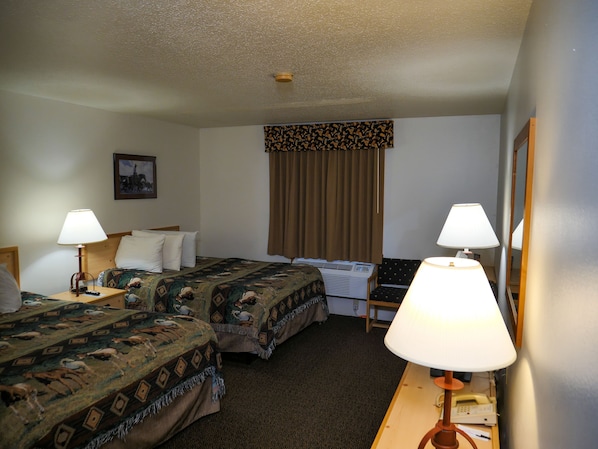 Quarto de hotel com duas camas de solteiro, uma escrivaninha com cadeira, abajur, telefone e janela com cortinas.