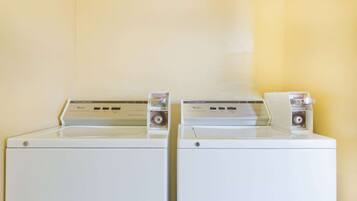 Duas máquinas de lavar Whirlpool brancas, lado a lado, em frente a uma parede amarela.