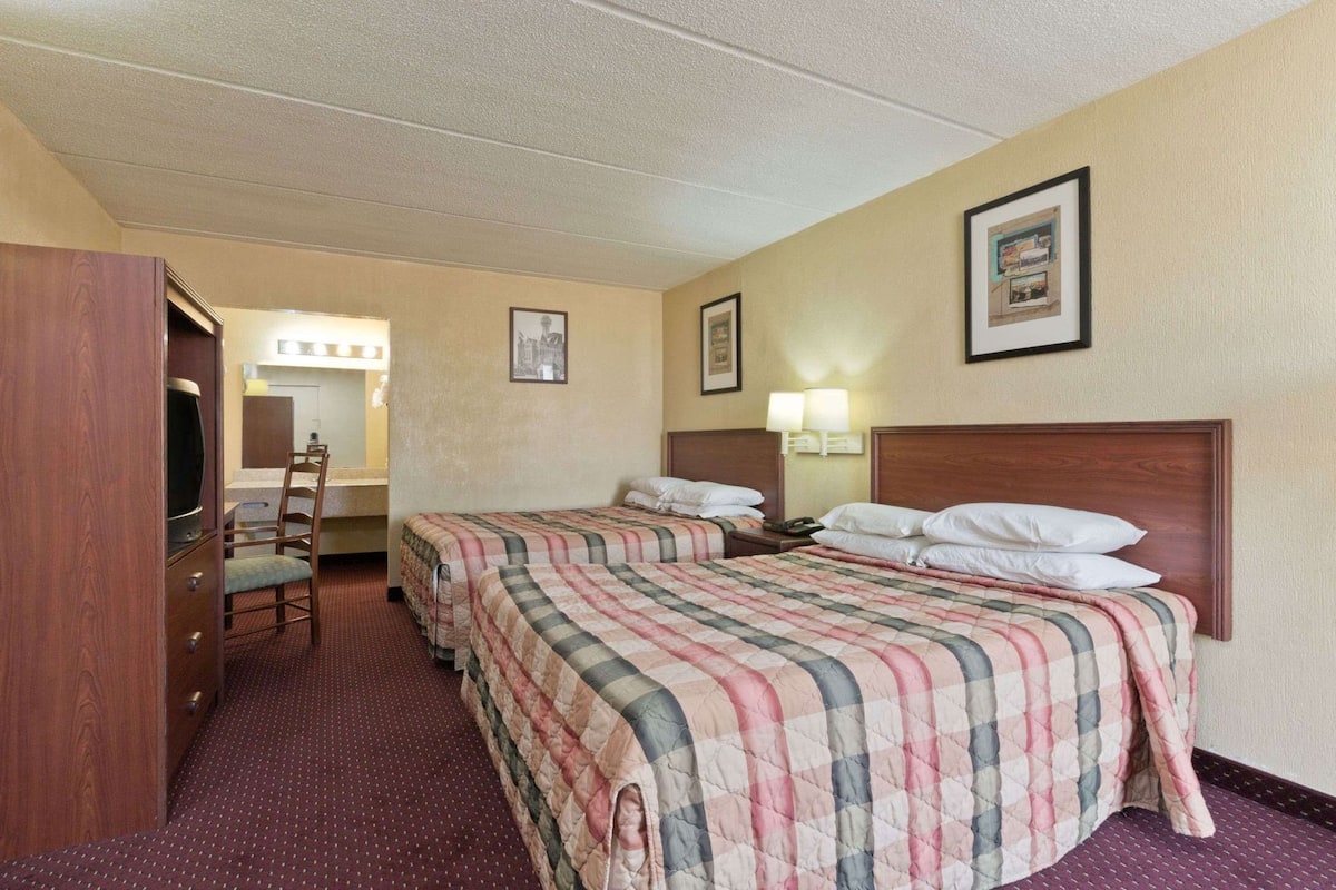 Quarto de hotel com duas camas, televisão, secretária e uma cadeira.