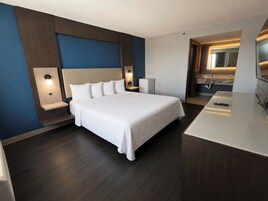 Quarto de hotel moderno com uma cama grande, mesas de cabeceira, TV integrada e um banheiro visível através de uma porta aberta.