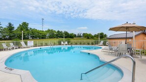 Uma piscina com grade de metal, rodeada por espreguiçadeiras e um guarda-sol.