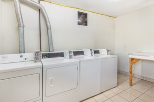 Uma lavanderia com quatro máquinas de lavar e secadoras Whirlpool, um aviso sobre sabão para roupa e uma mesa de madeira.