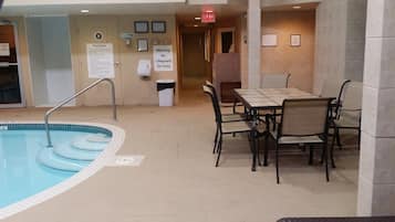 Uma área de piscina com uma placa indicando as regras da piscina, uma placa indicando a presença de salva-vidas e uma mesa com cadeiras.
