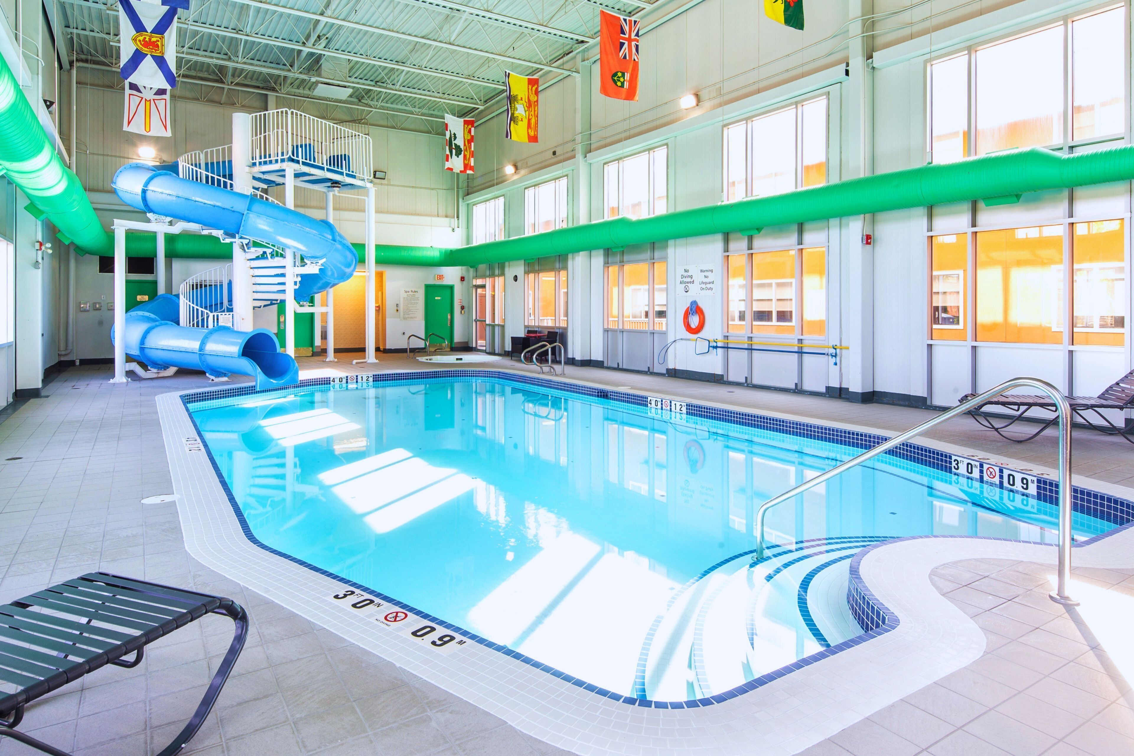 Uma piscina interior com um tobogã azul, um trampolim e várias bandeiras.