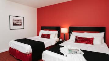 Quarto de hotel com duas camas, cada uma com roupa de cama branca e detalhes vermelhos, um quadro na parede e piso coberto por um tapete vermelho.