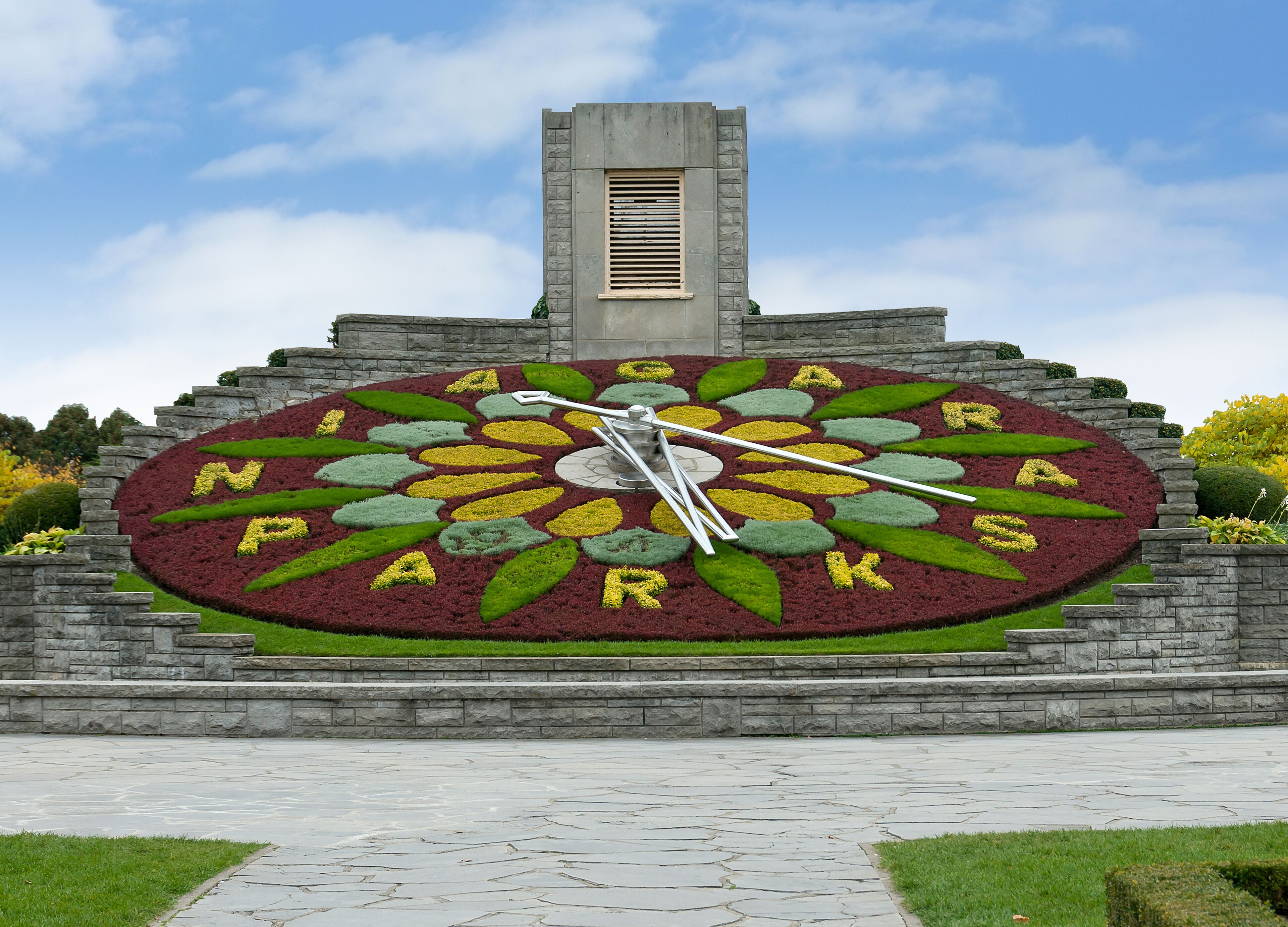 Um relógio grande ao ar livre com as palavras "NAPA PARKS" no mostrador, rodeado por um jardim paisagístico.