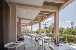 Um café ao ar livre com mesas e cadeiras, grandes janelas e vista para a cidade.