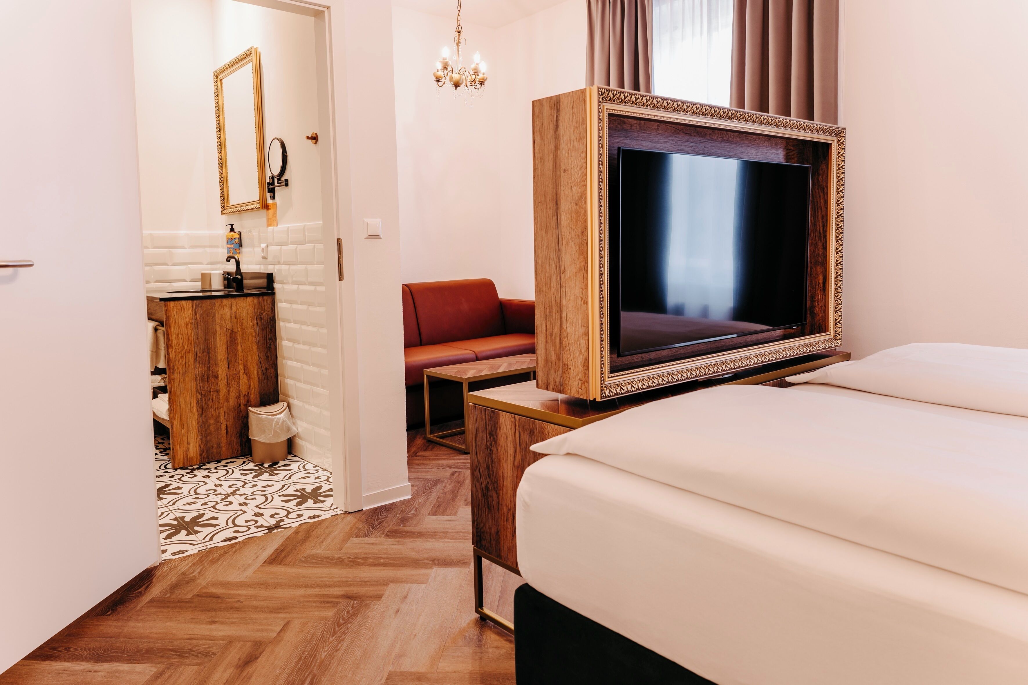 Quarto de hotel com cama, televisão sobre suporte de madeira, cadeira vermelha, penteadeira de madeira e tapete estampado.