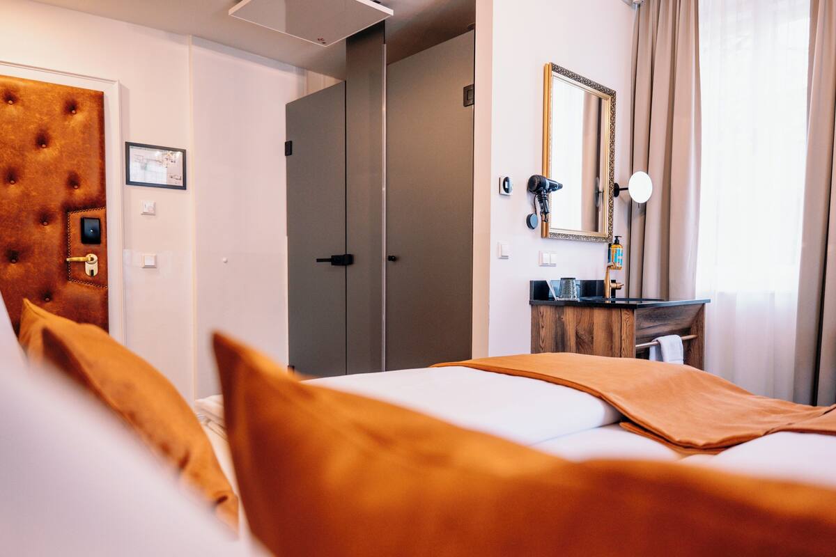 Quarto de hotel com cama, guarda-roupa, espelho e secretária com candeeiro.