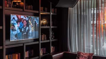 Uma sala de estar aconchegante com uma grande TV de tela plana, sofá de couro, estantes de livros e uma mesa de centro.