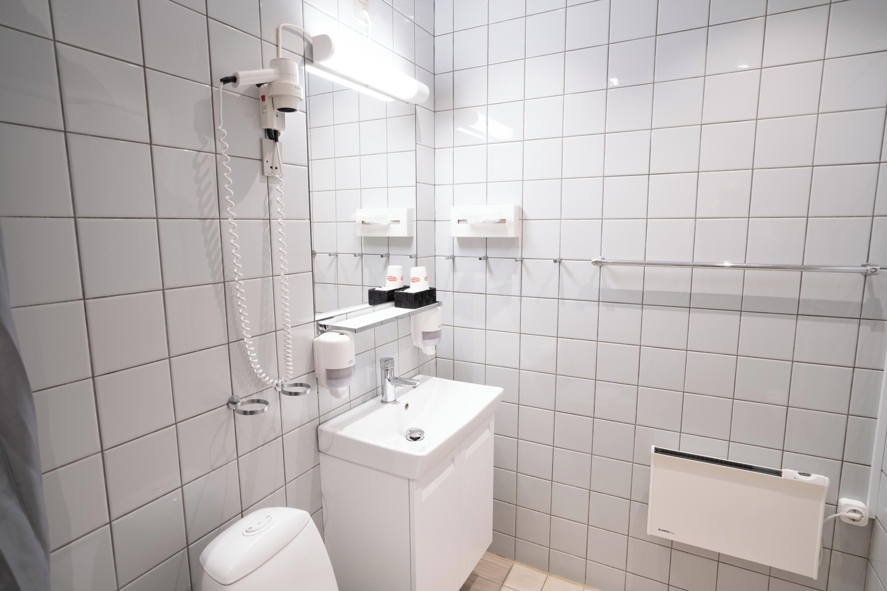 Um banheiro moderno com azulejos brancos, pia branca, vaso sanitário, chuveiro manual e porta-toalhas.
