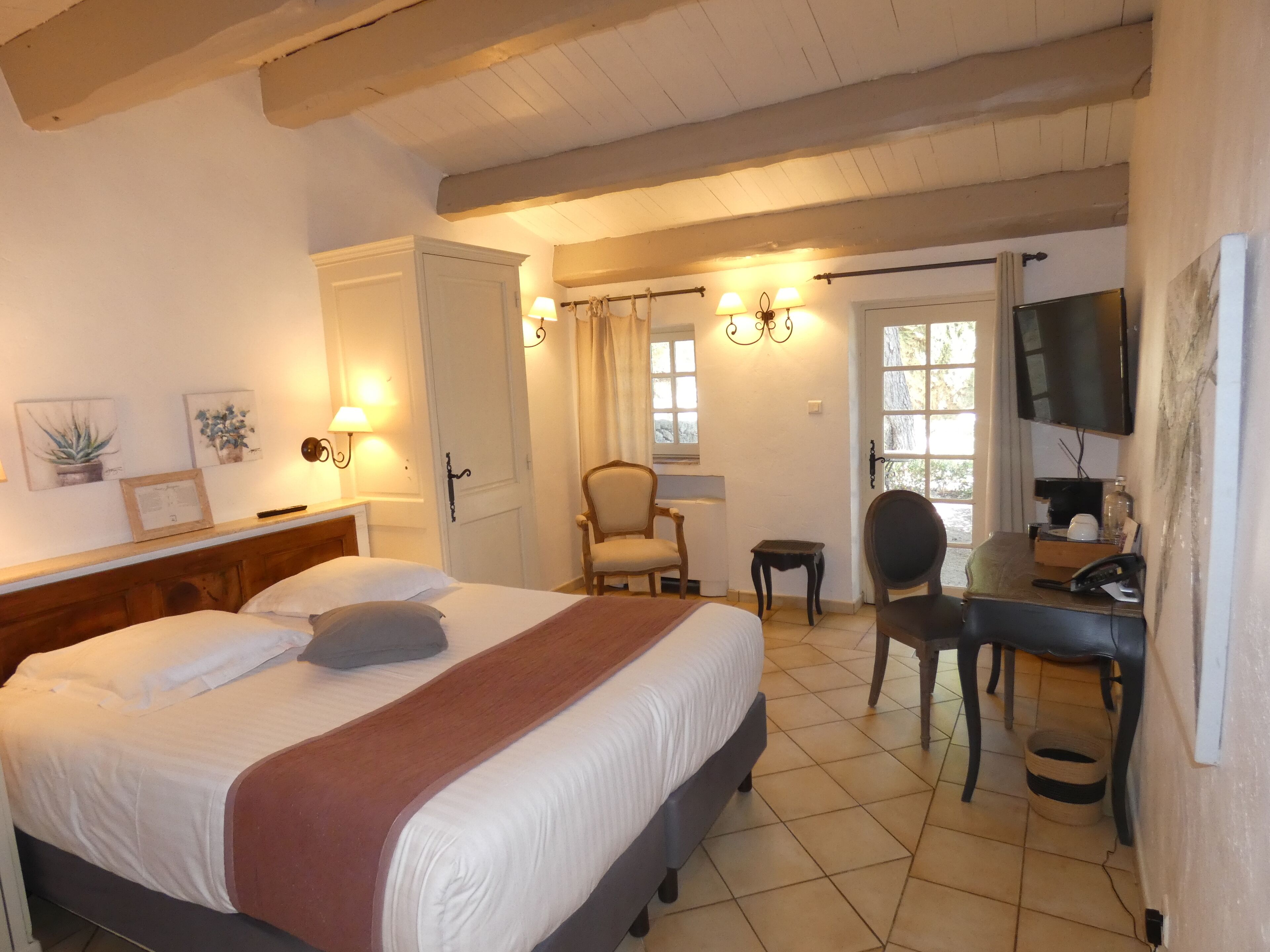 Quarto com cama, mesa de cabeceira, abajur, cadeira, escrivaninha e televisão.