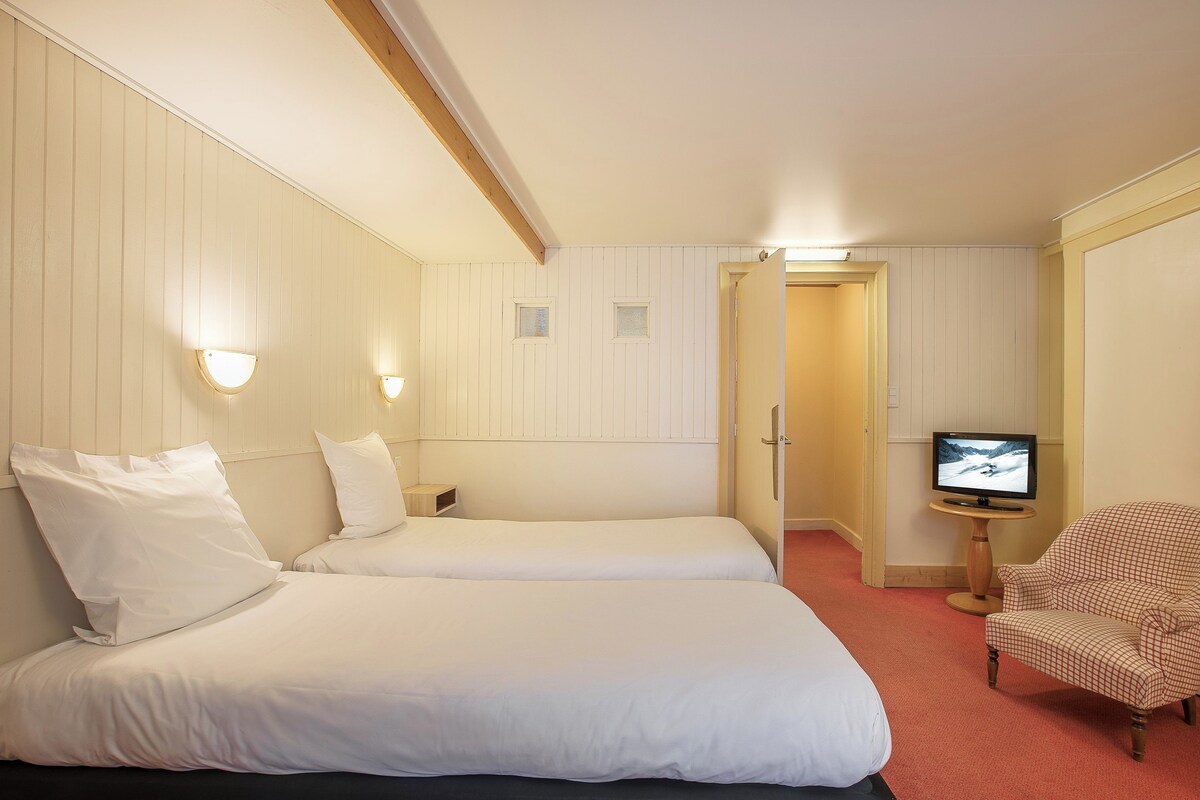 Quarto de hotel com duas camas, televisão, uma cadeira e uma mesa pequena.