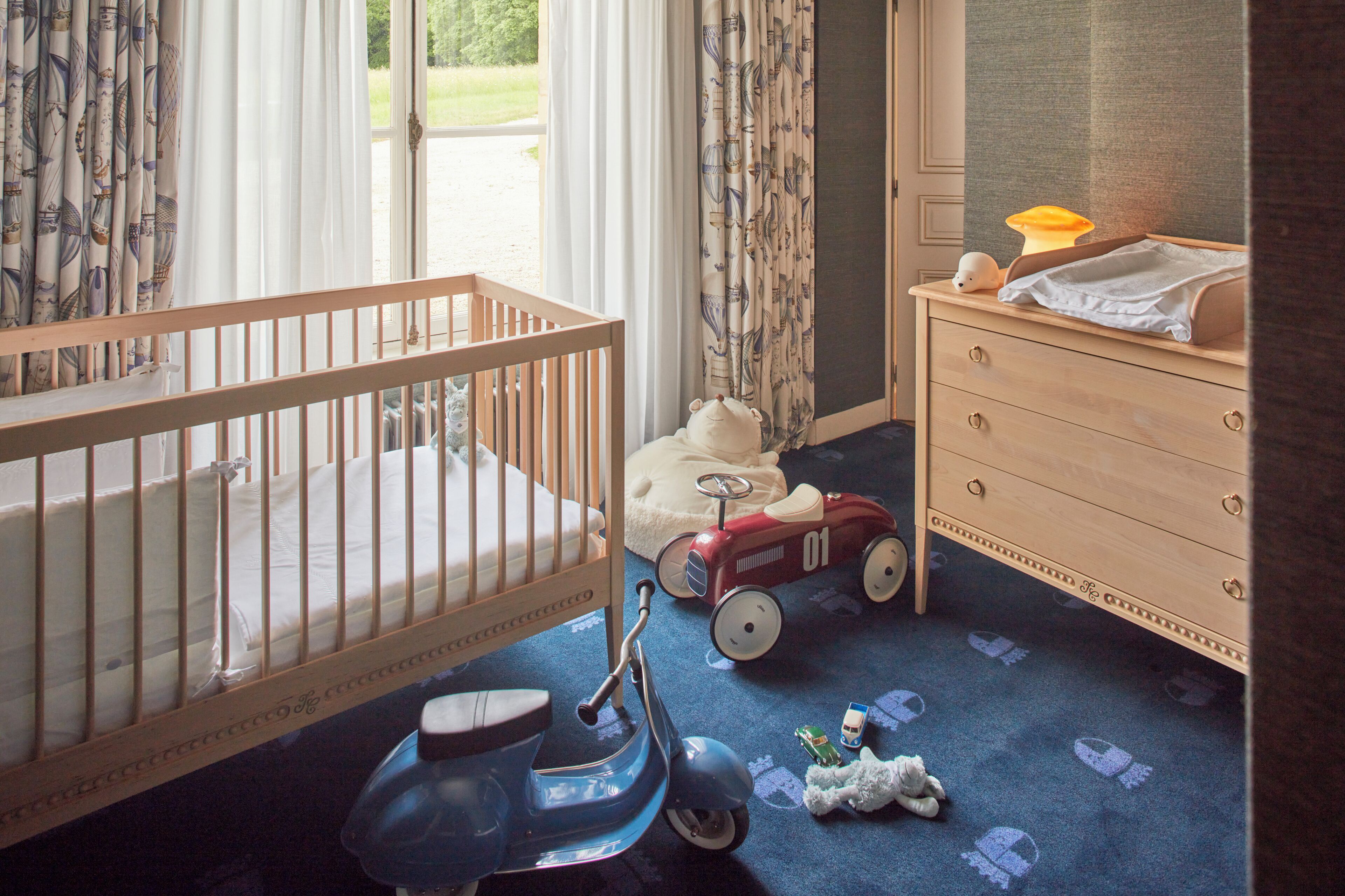 Quarto infantil com berço, cômoda, um carrinho de brinquedo e um patinete.
