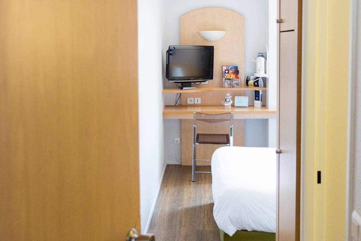 Quarto de hotel com uma cama, uma secretária com televisão e uma porta com o número 106.