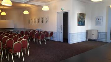 Uma sala de conferência com fileiras de cadeiras vermelhas, uma mesa comprida e iluminação pendente.