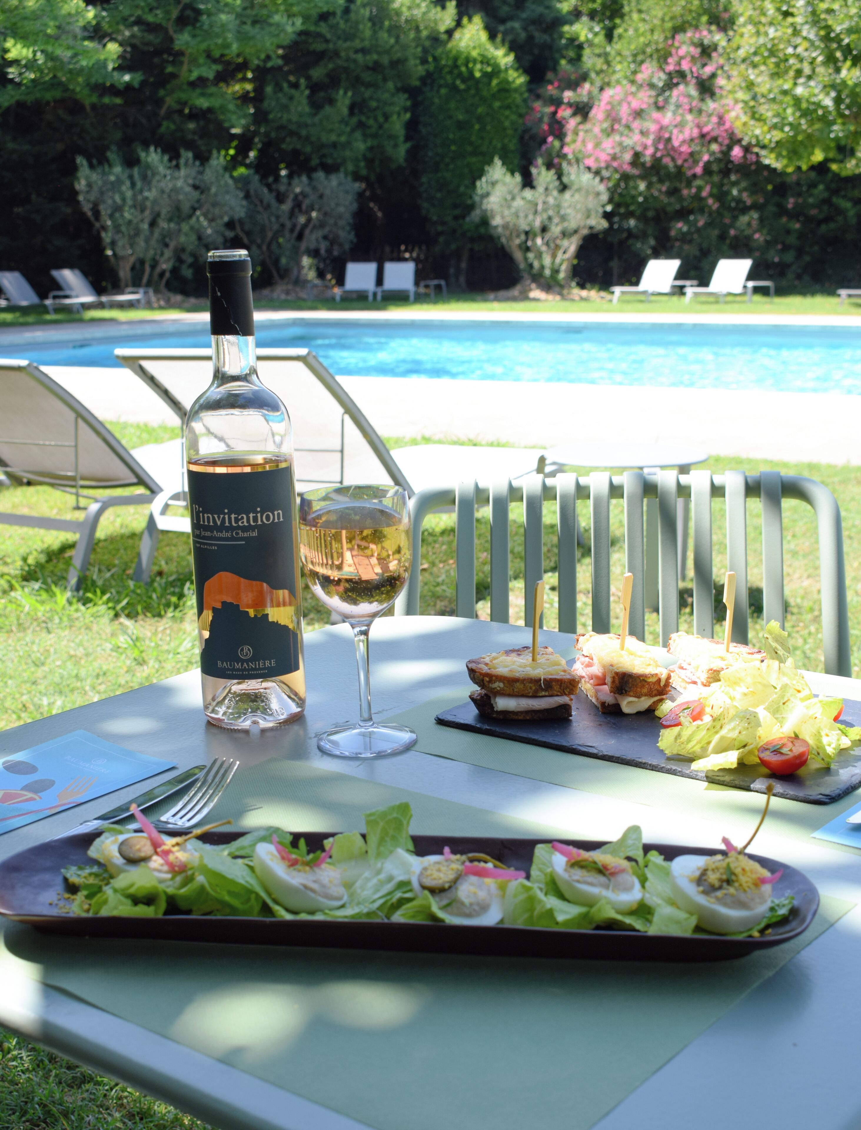 Mesa de jantar com garrafa de vinho, um copo, sanduíches e uma bandeja de salada.
