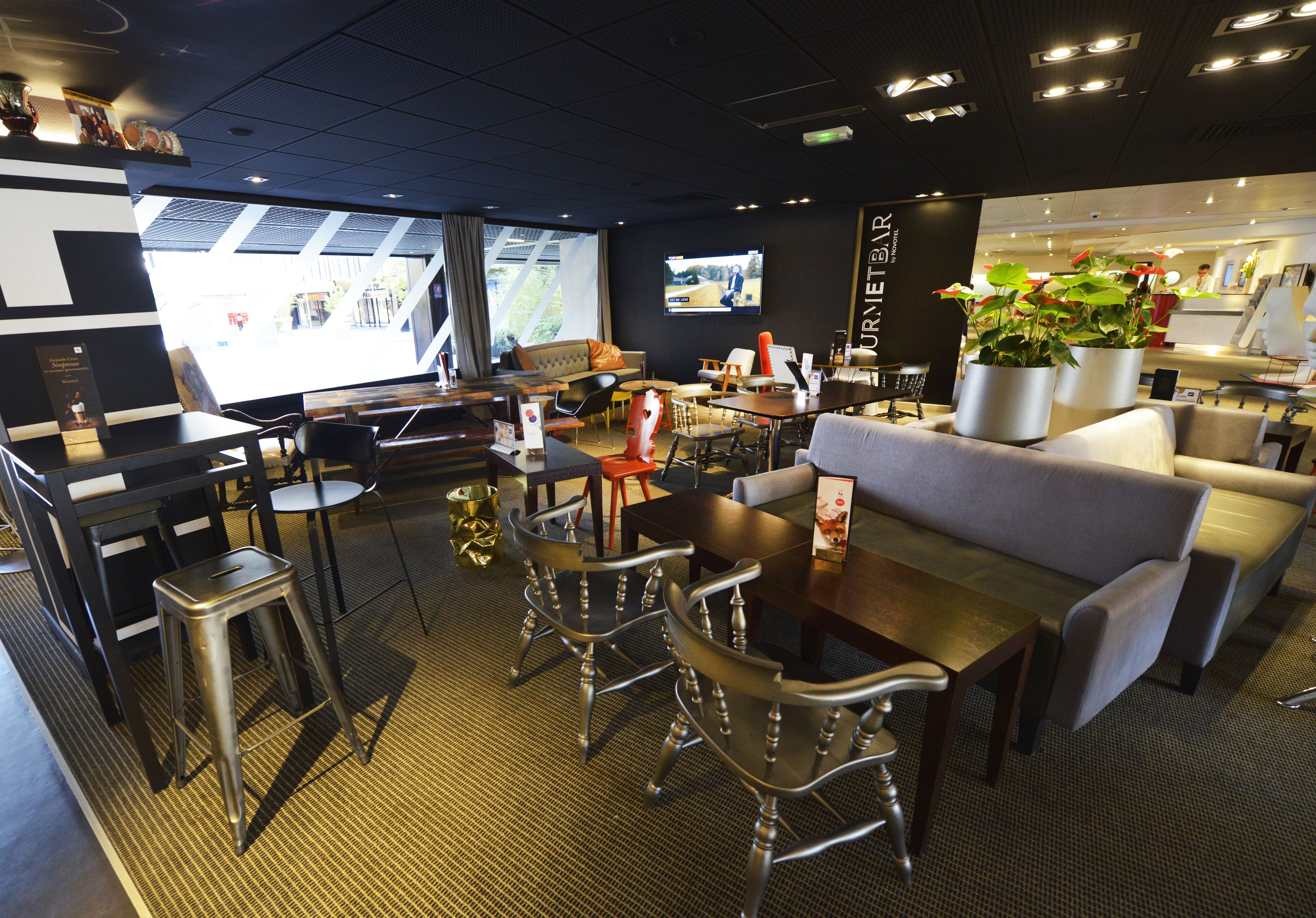 Uma área de bar moderna com assentos, uma tela de televisão e um balcão.