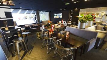 Uma área de bar moderna com assentos, uma tela de televisão e um balcão.